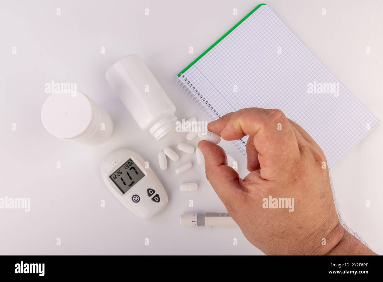 A glucose meter, note pad, white pills, and a hand taking a pill are ...