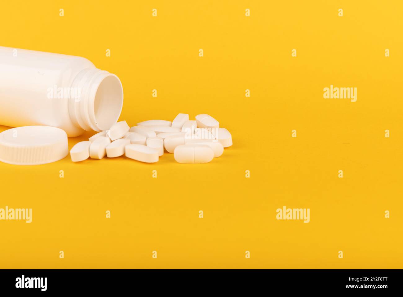 Overturned white medication bottle with tablets spread across a bright ...
