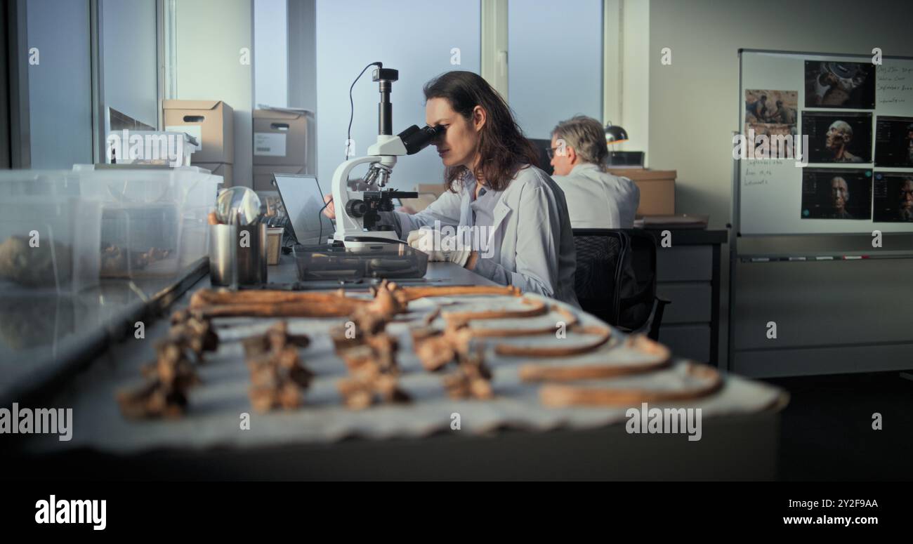 Female scientist analyzes sample of fossil remains under microscope ...