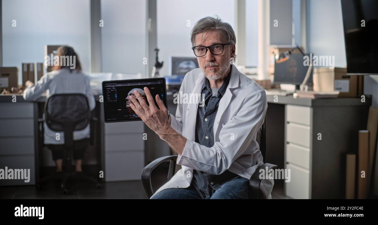 Mature scientist speaks to camera, shows 3D model of human head on ...