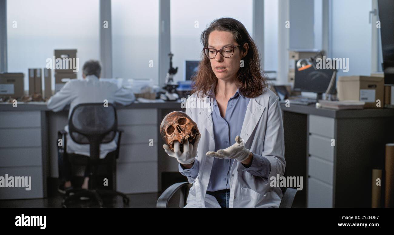 Female scientist speaks to camera, shows fossil skull of prehistoric ...