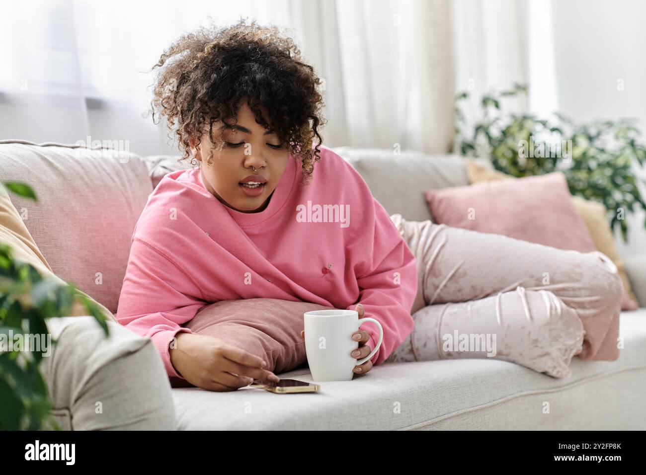 A young woman sips tea while lounging comfortably on the couch Stock ...