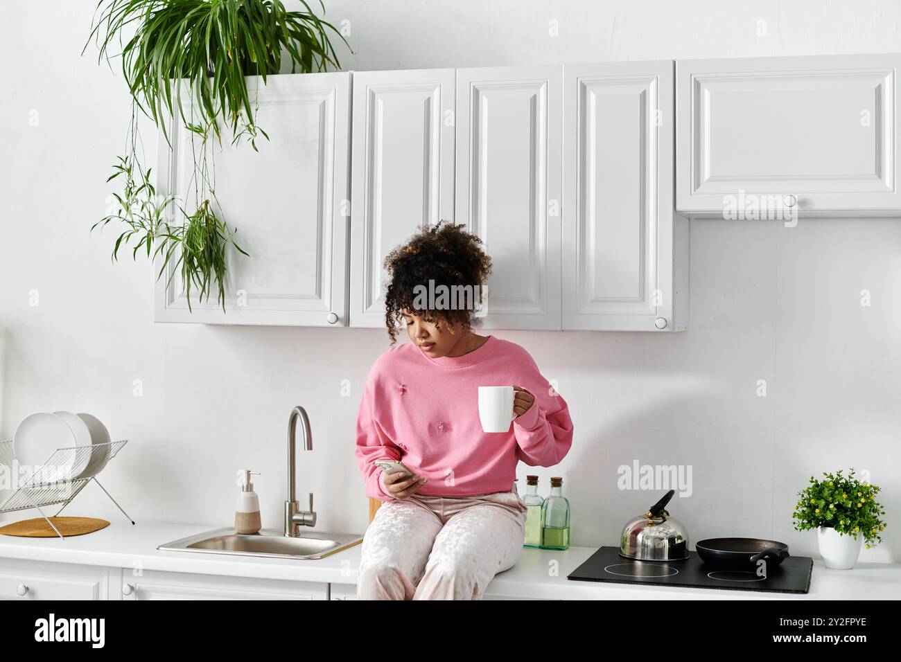 A young woman sips tea while sitting on her kitchen counter Stock Photo ...