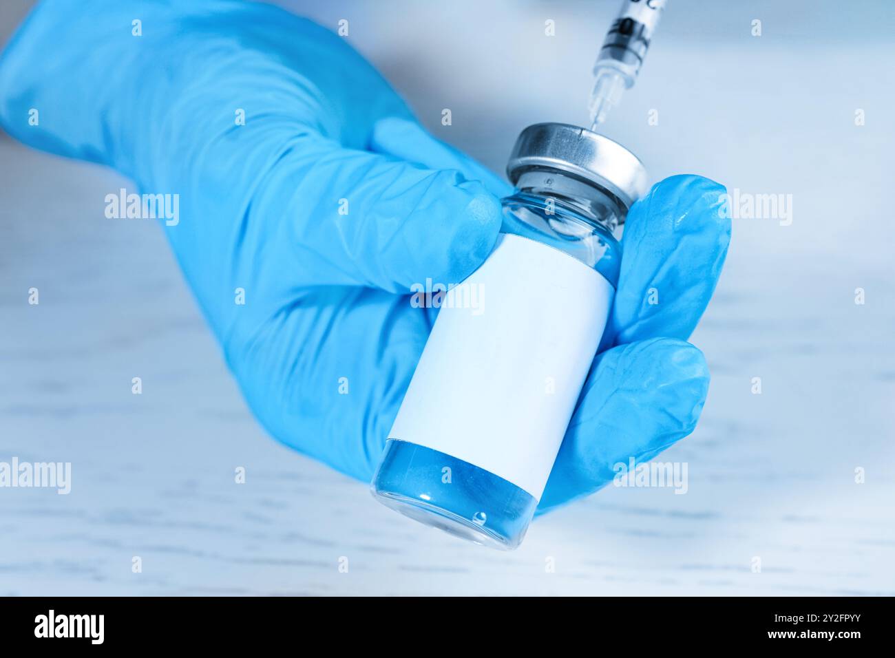Nurse filling syringe with medication from vial at white wooden table ...