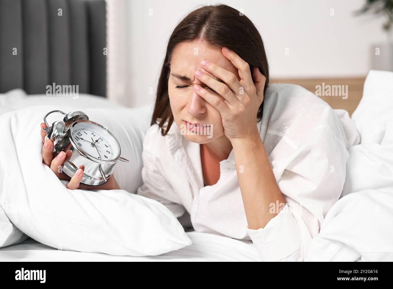 Sleepy woman waking up with alarm clock in bed at lunch time Stock ...