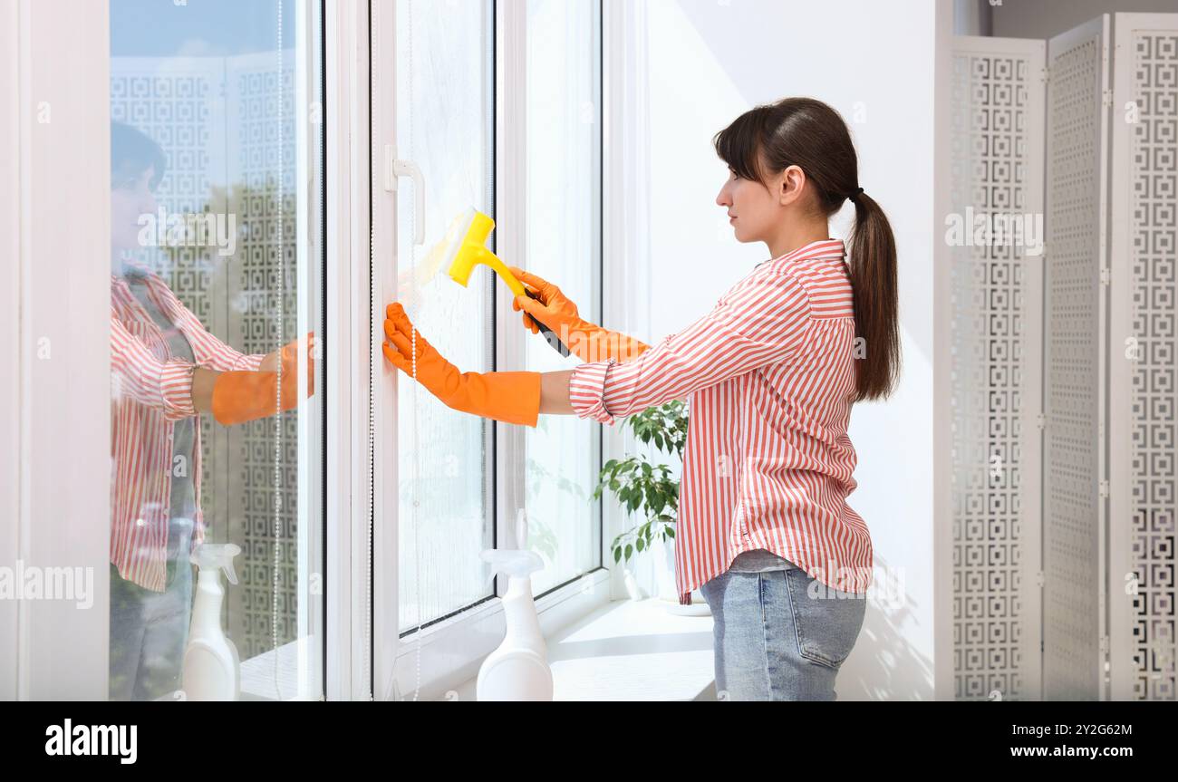 Beautiful young housewife with squeegee cleaning window indoors Stock ...