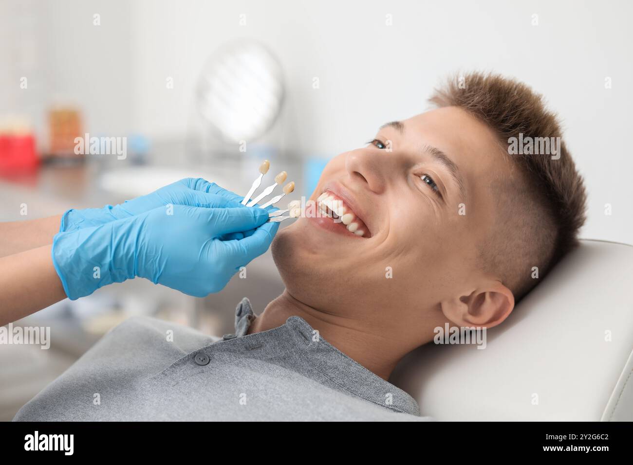 Doctor checking young man's teeth color in clinic, closeup. Dental ...