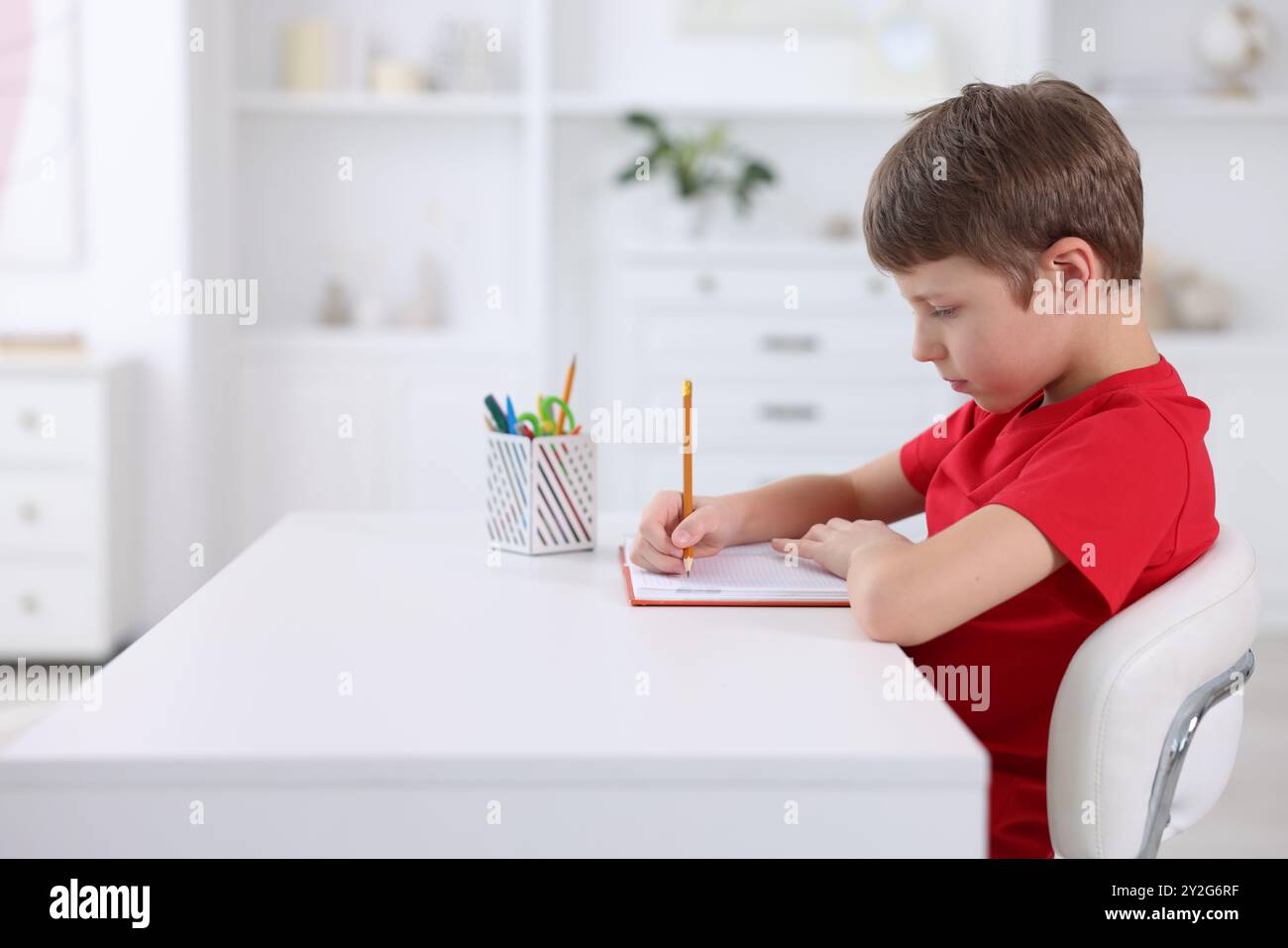 Boy with correct posture doing homework at white desk indoors Stock ...