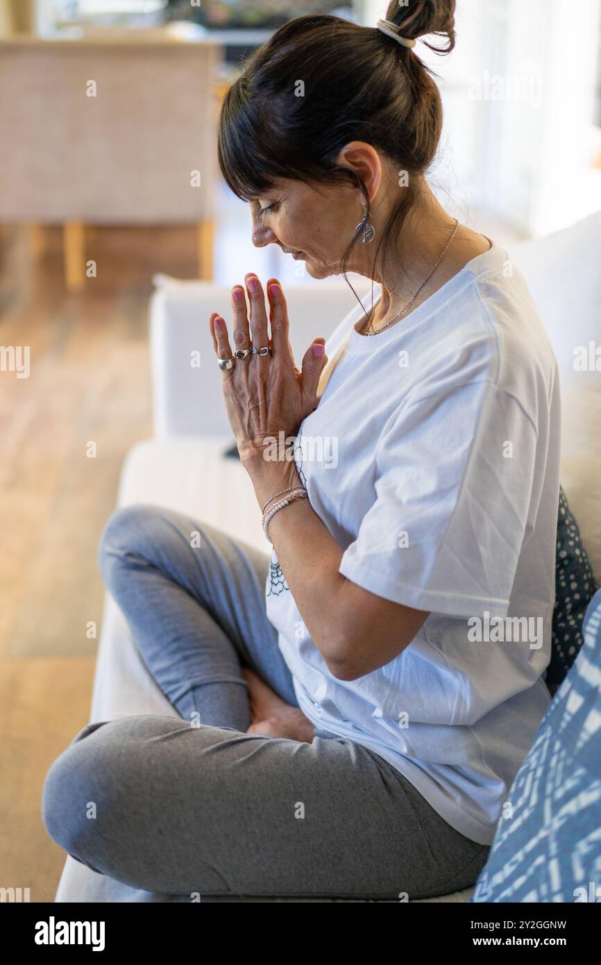 Side view of a mid-adult woman meditating on her sofa at home, with ...