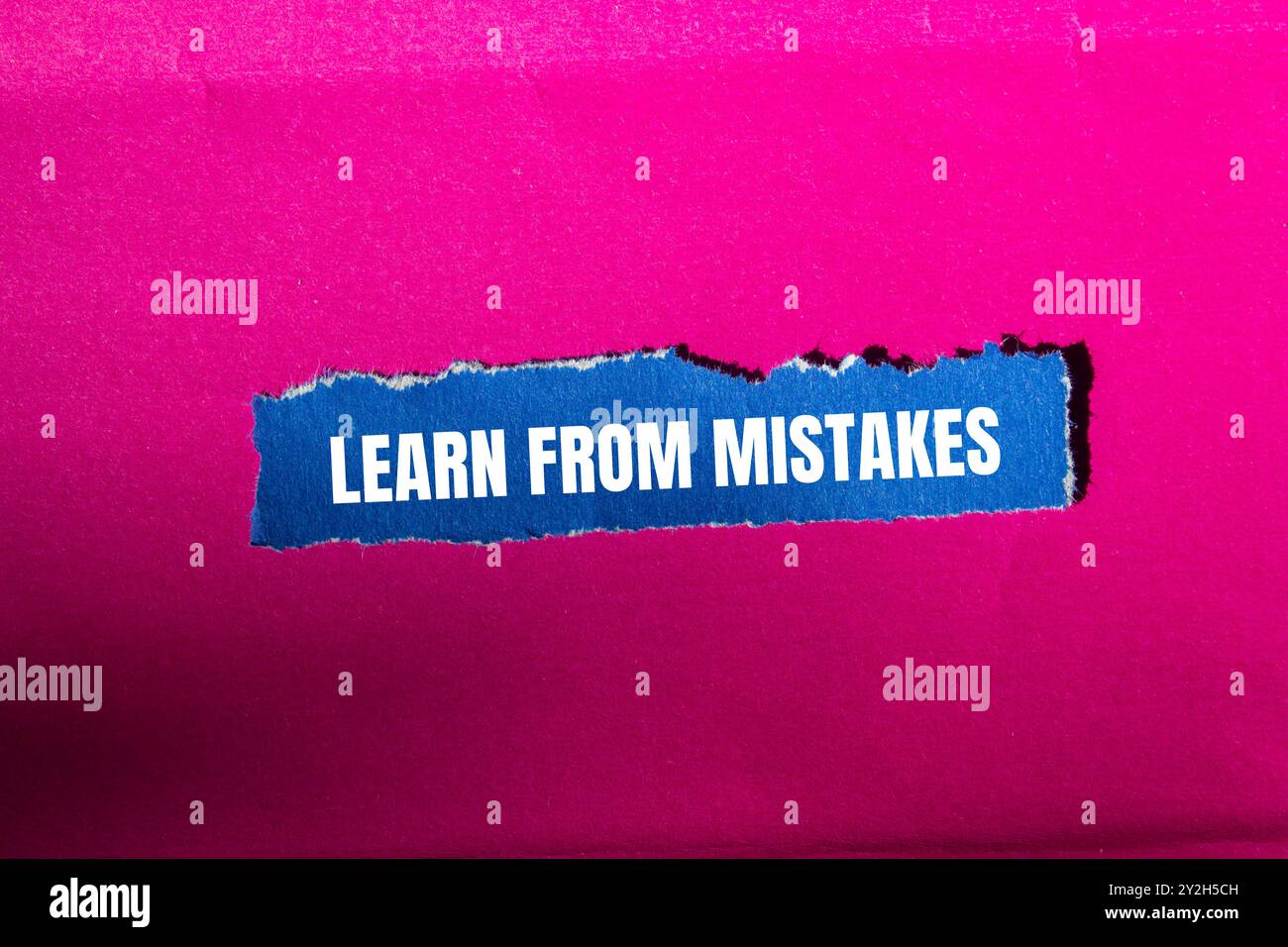 Learn from mistakes message written on ripped torn blue paper piece with pink background ...