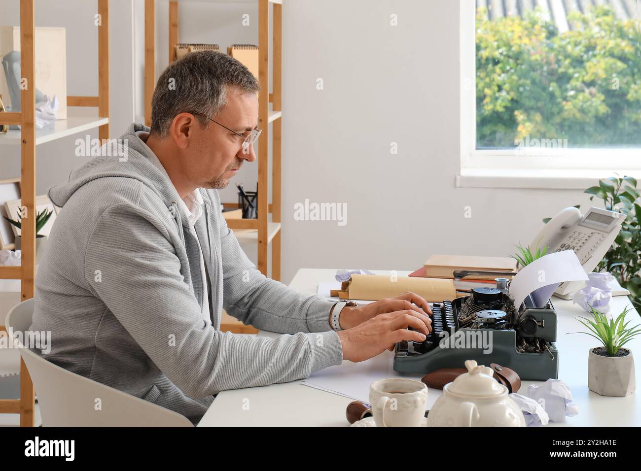 Mature man with scroll and paper sheets typing on vintage typewriter at ...