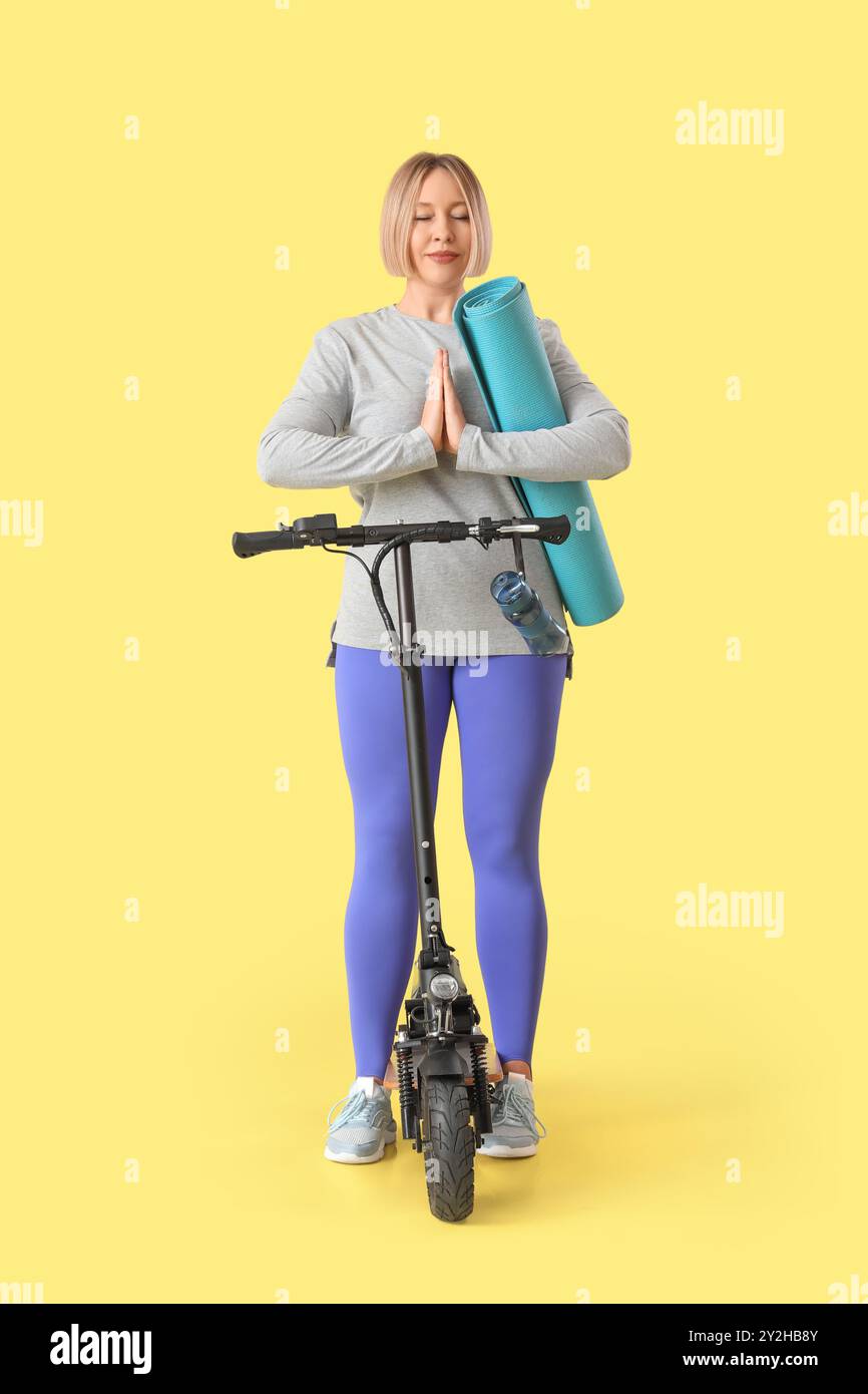 Beautiful mature sporty woman with kick scooter and yoga mat on yellow background Stock Photo ...