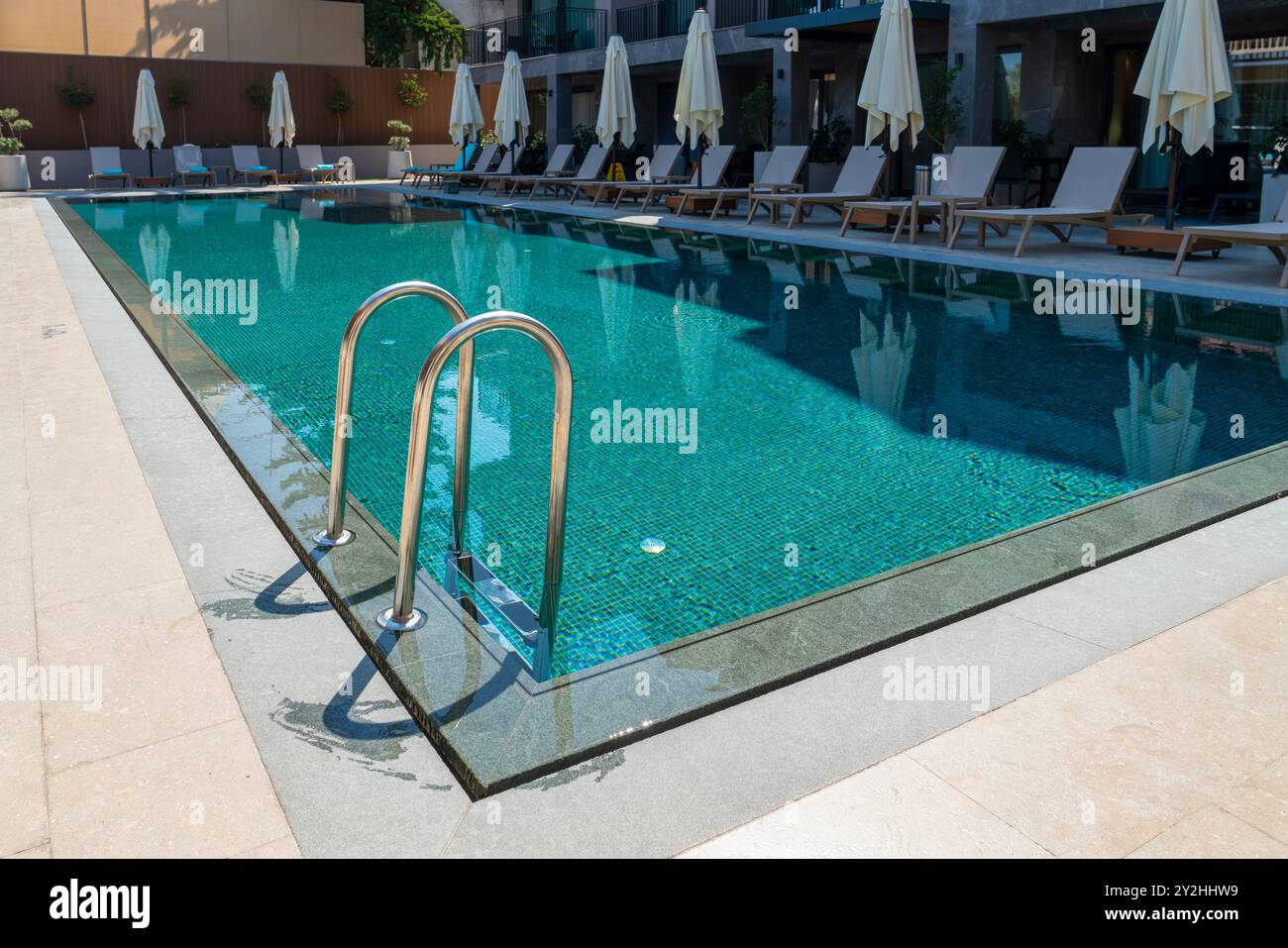 A rectangular swimming pool with sun loungers, parasols and towels with ...
