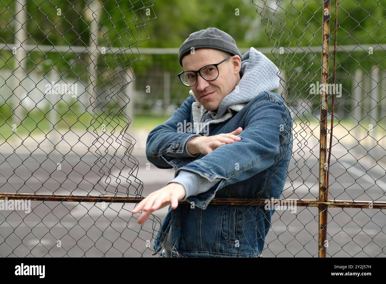 A Man with glasses in a Denim Jacket Dances Near a Chain Link Fence ...