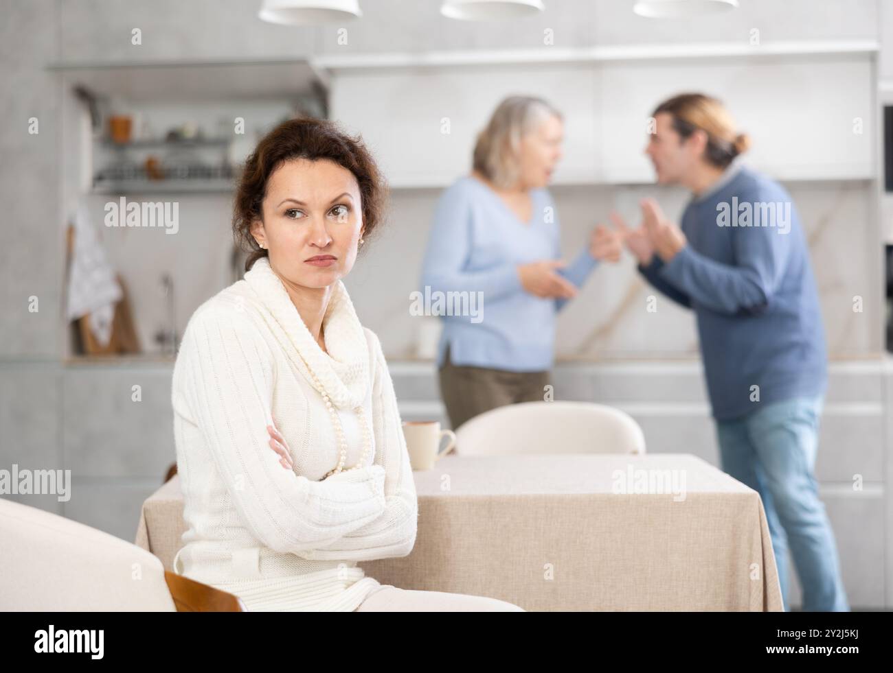 Sad thinking woman sits in kitchen and listens to man quarrel with ...