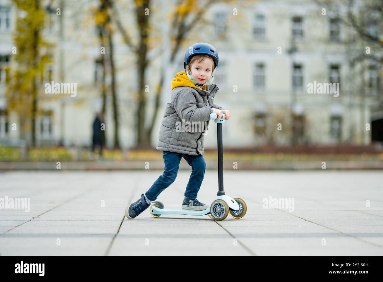 Adorable little boy riding his scooter in a city on autumn day. Young ...