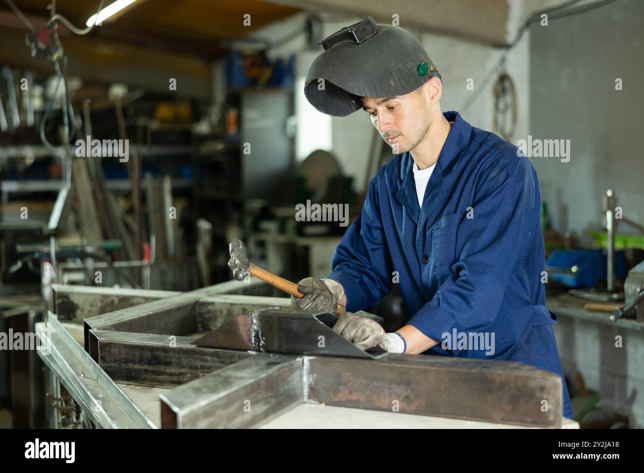 Male welder standing with a welding semi-automatic machine and a safety helmet in metal ...