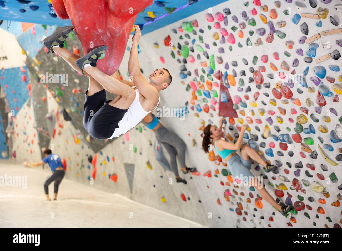 Young man and two women engaged in rock-climbing in indoor hangar Stock ...