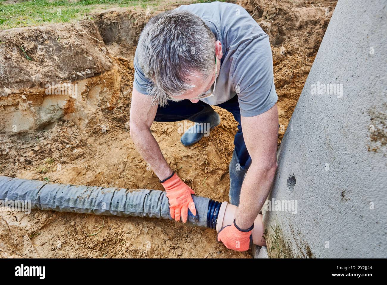 Worker connects perforated drain pipe to septic tank through which ...