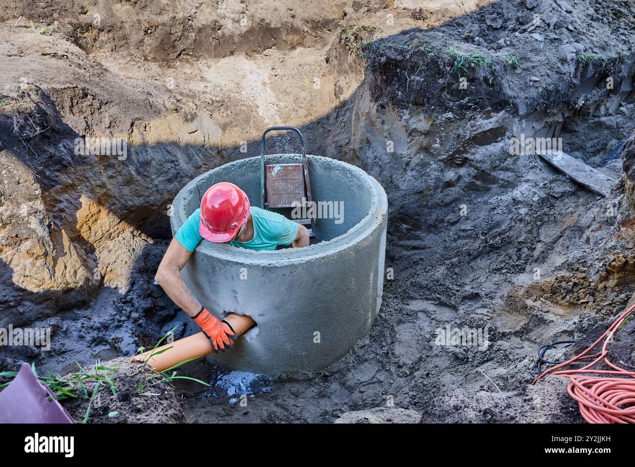Worker connects sewer pipe to hole in concrete ring of septic tank ...