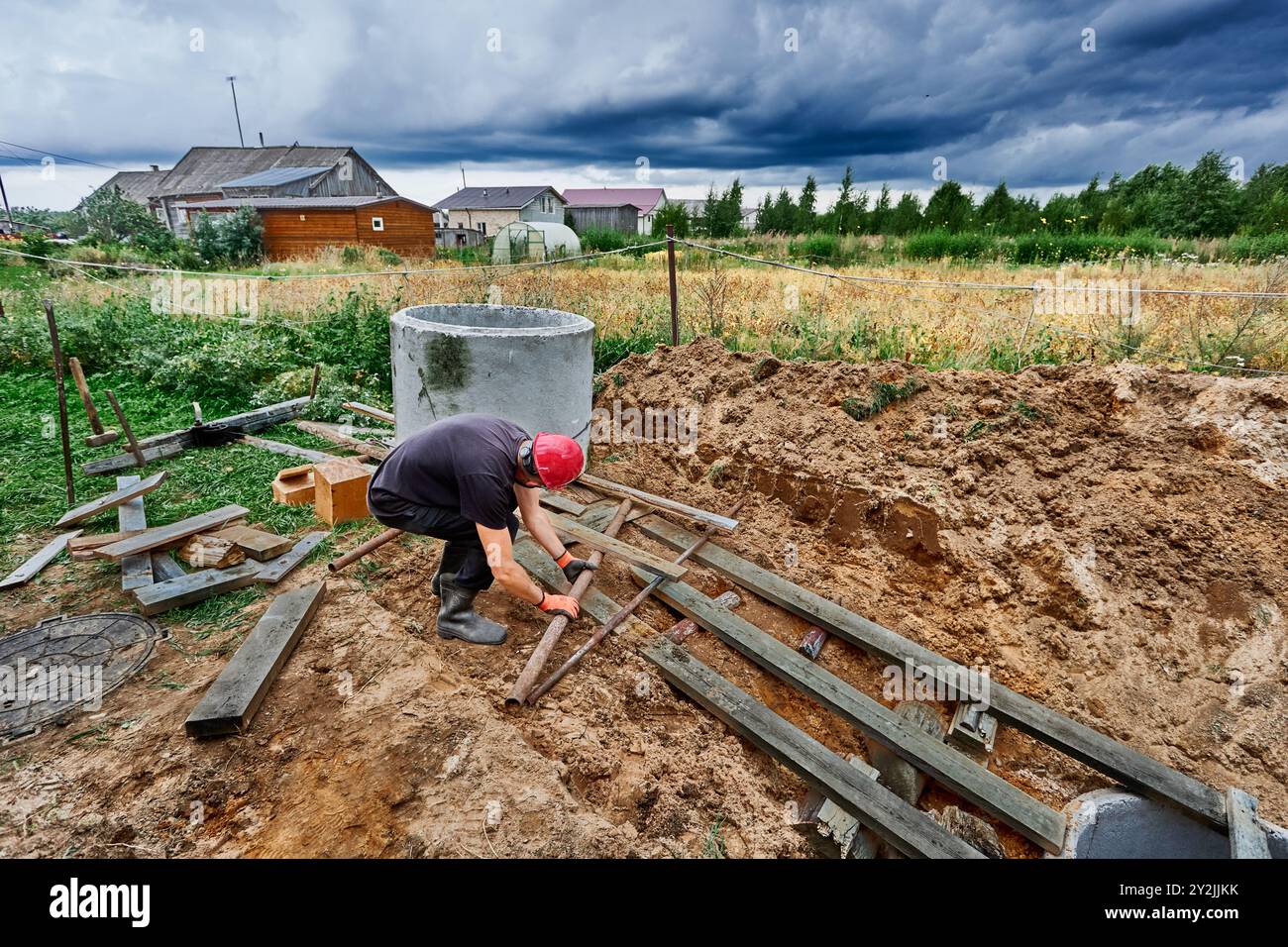 Worker moves concrete ring along wooden platform with steel pipe ...