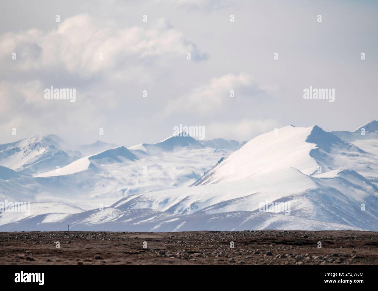Snow covered mountains in background with dry rocky ground in ...