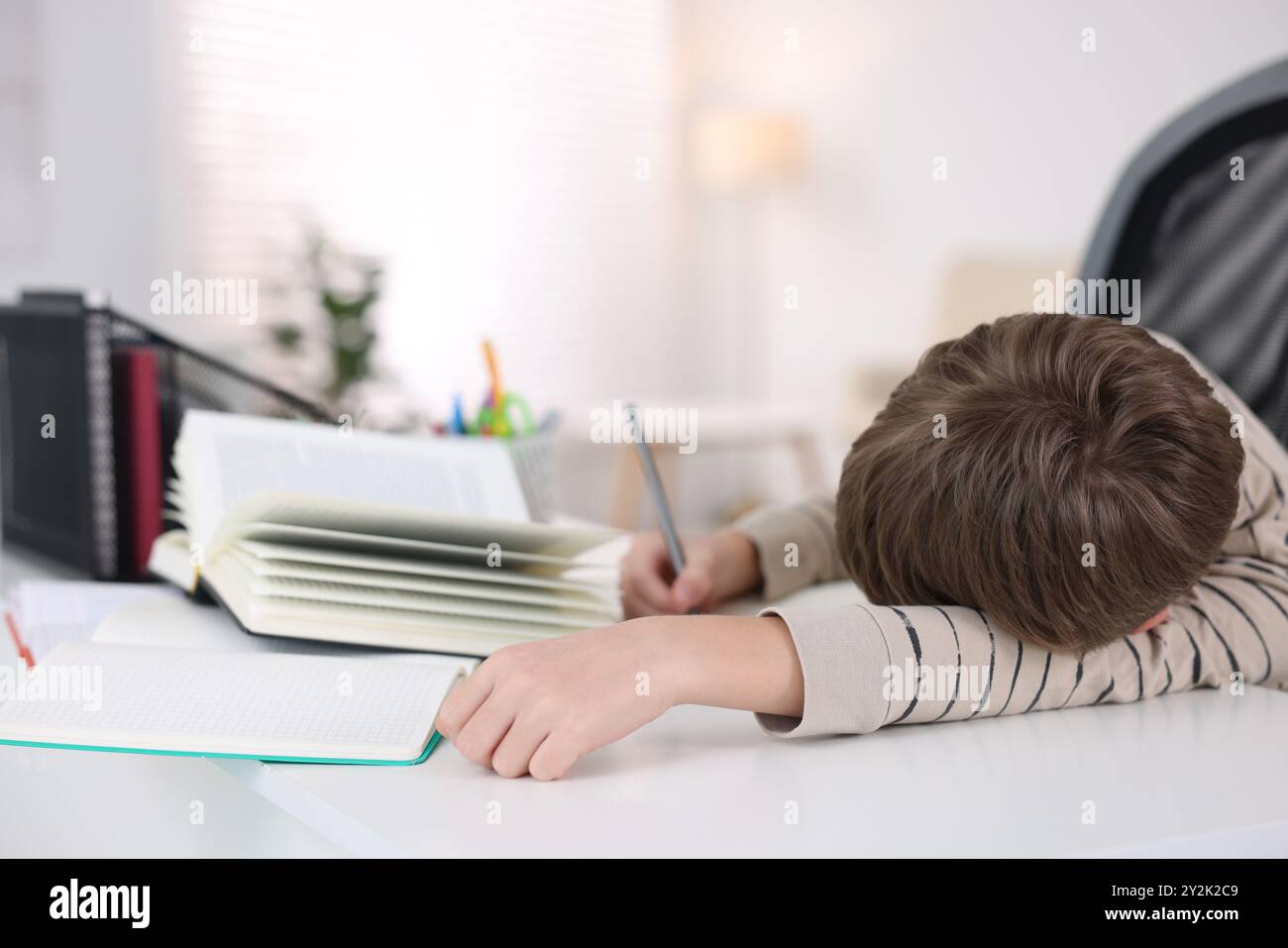 Boy with incorrect posture doing homework at white desk indoors Stock ...