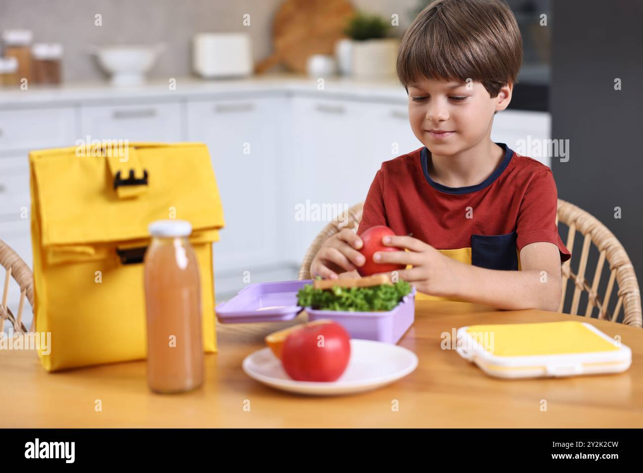 Cute boy with lunch box, healthy products and bag at wooden table in ...