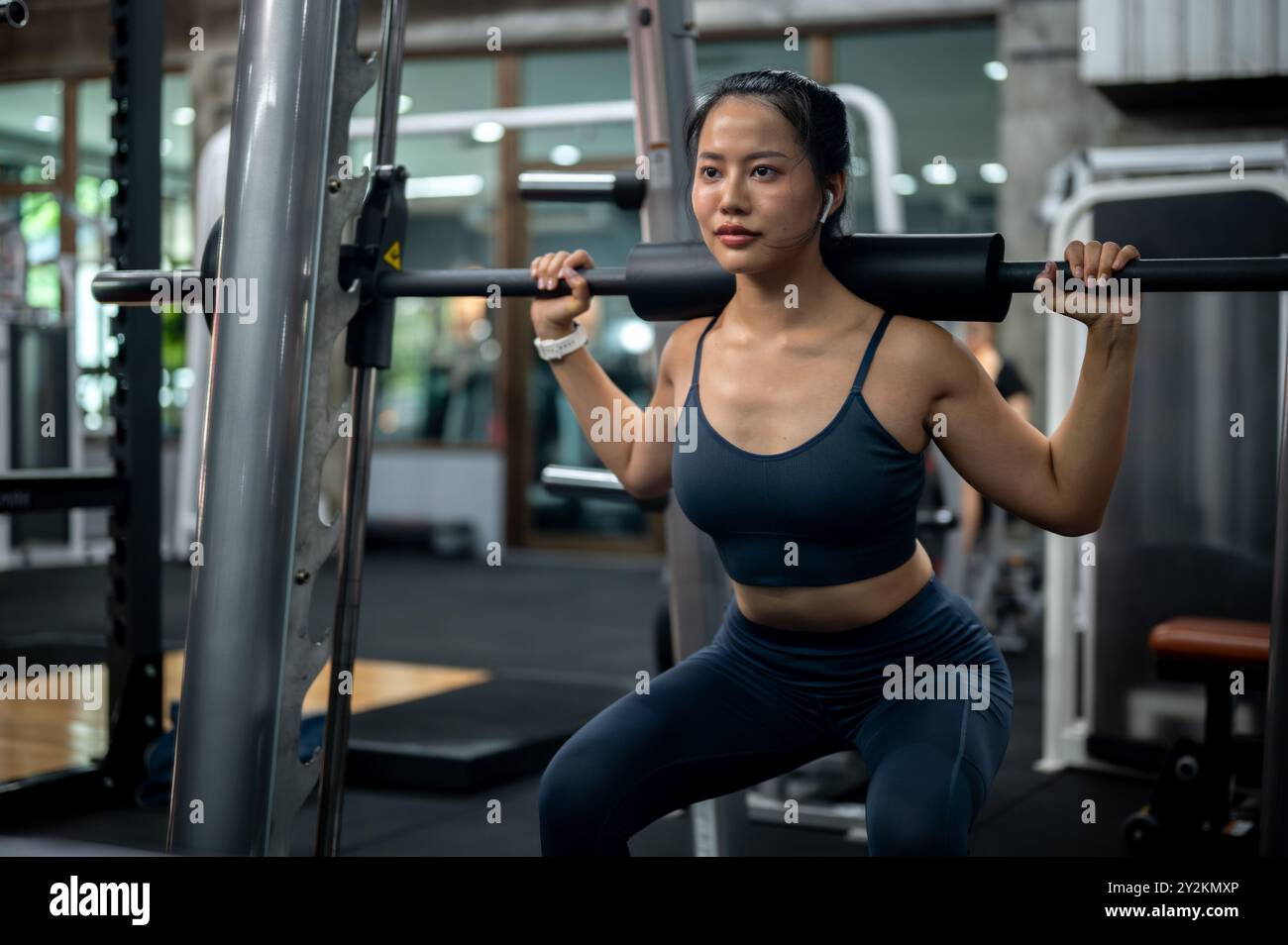 A sporty, strong Asian woman in athletic wear is performing squats on ...
