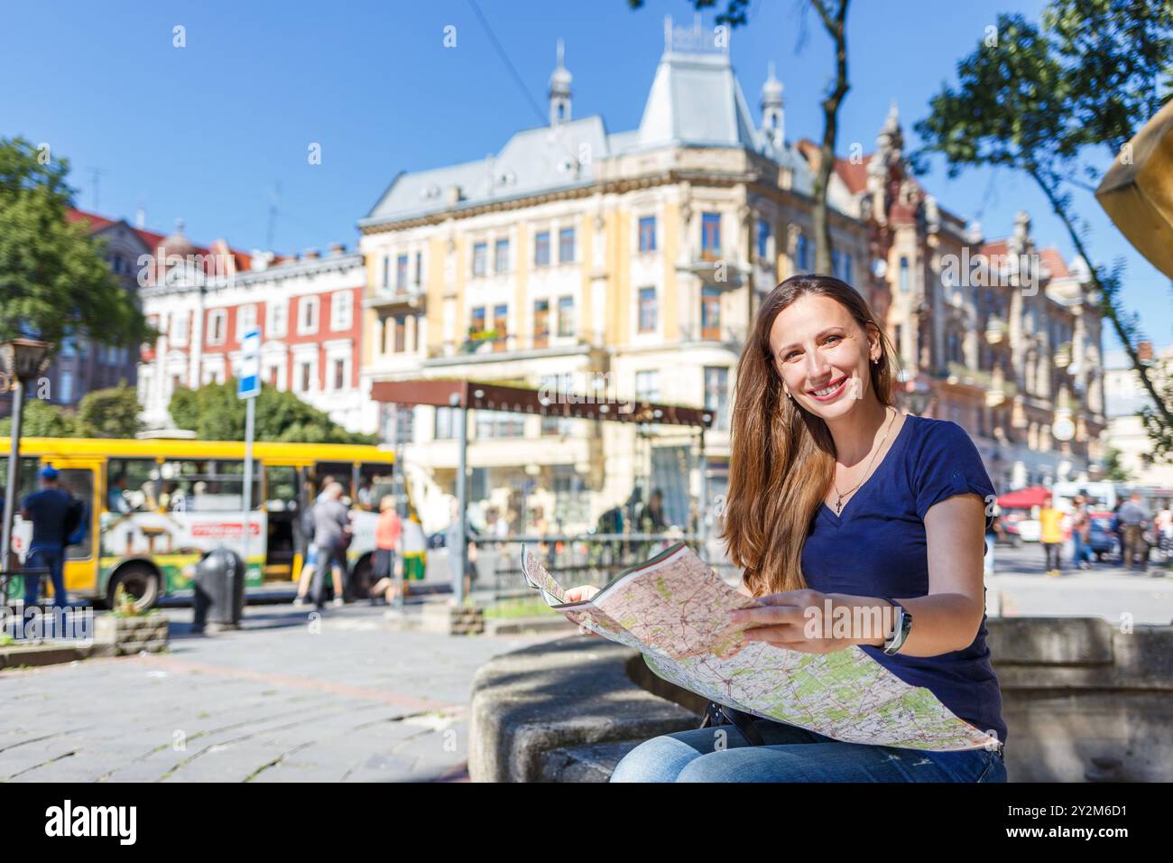A woman sits outside, happily examining a map while enjoying the sunny ...