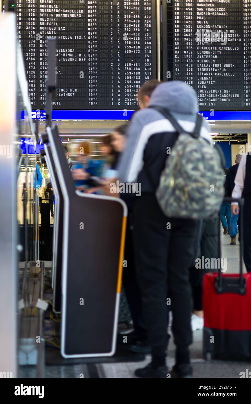 A line of travelers waits at an airport self-service kiosk for check-in ...