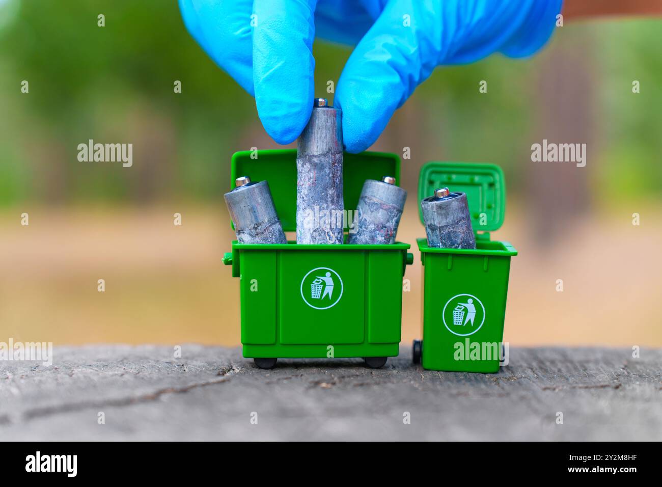 Hand adding heavily corroded batteries to miniature recycling bins ...