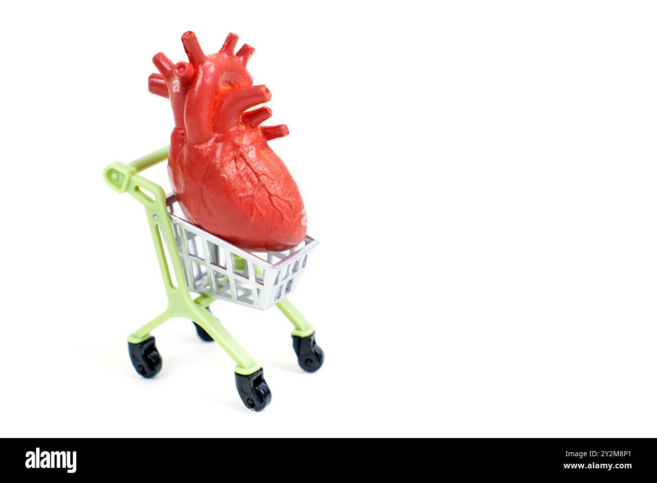 Clay heart model in a miniature shopping cart against a white ...