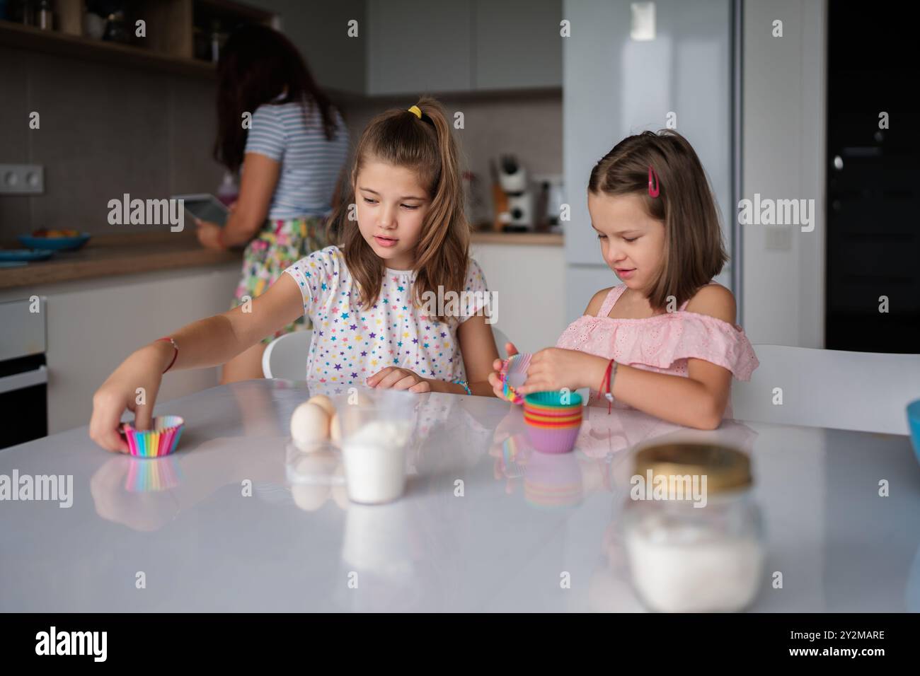 Two young girls baking cupcakes together in a modern kitchen Stock ...