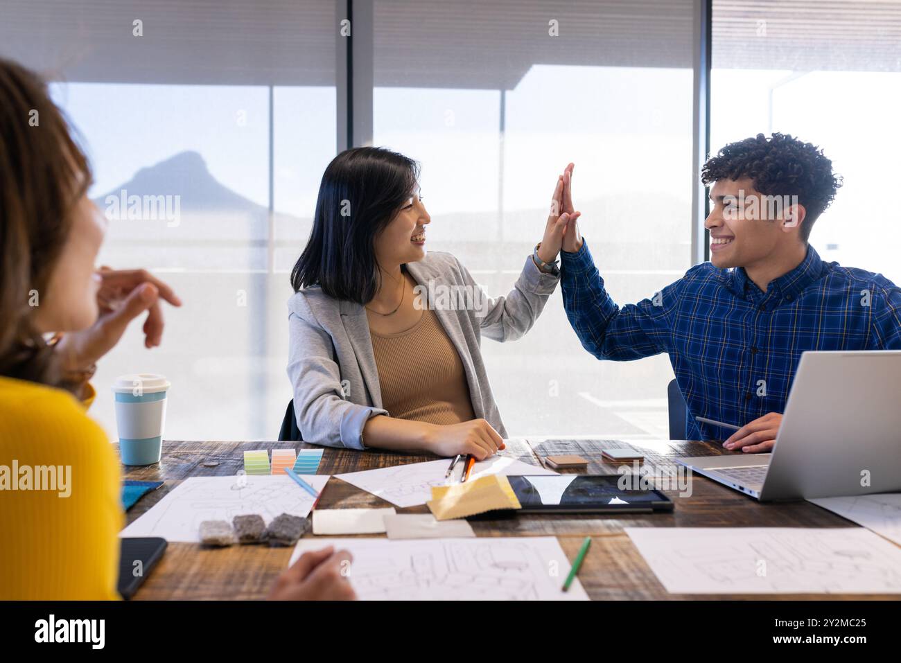High-fiving, diverse colleagues celebrating success with laptop and ...