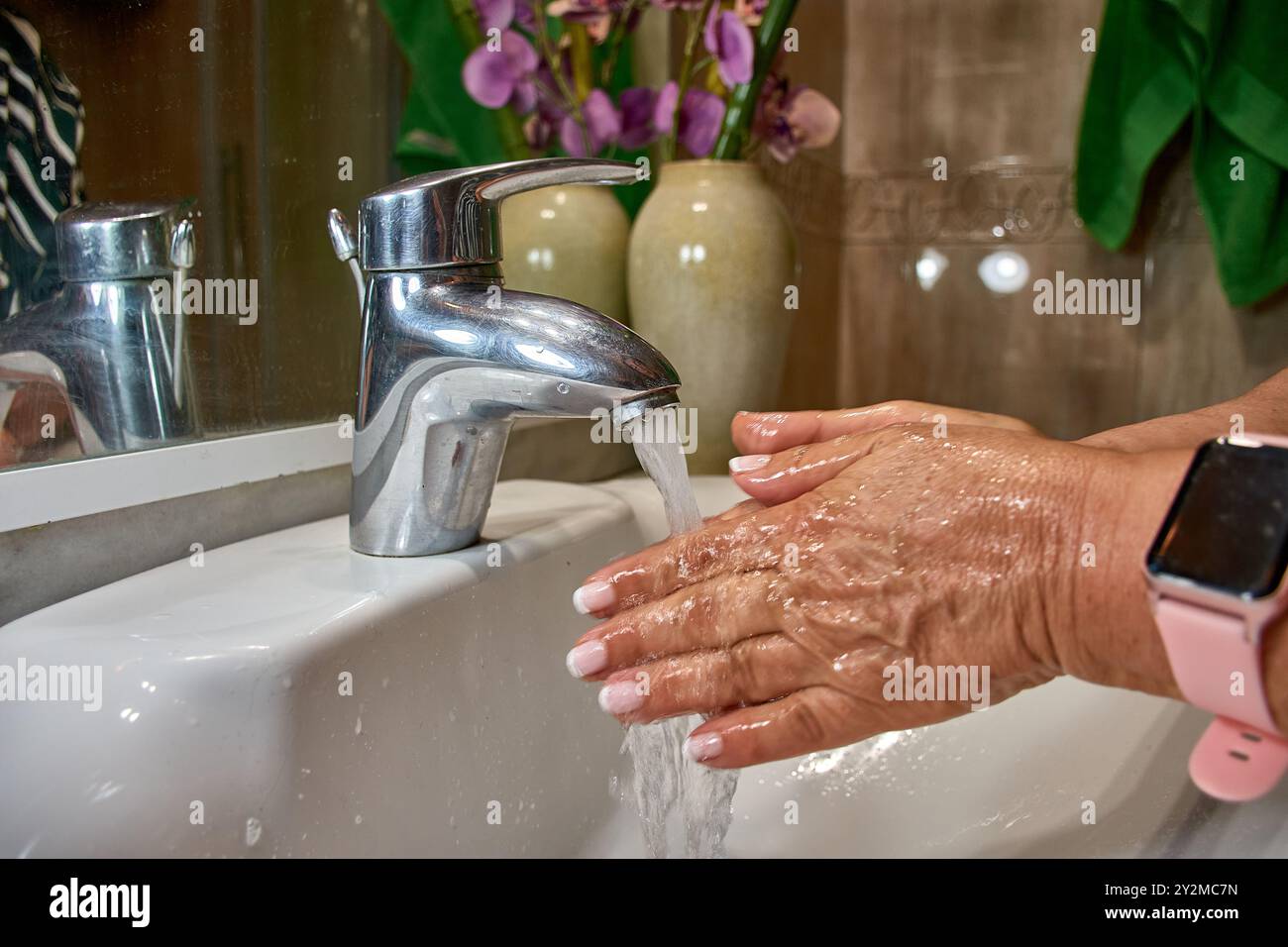 A woman washing her hands under running water in a modern bathroom sink ...