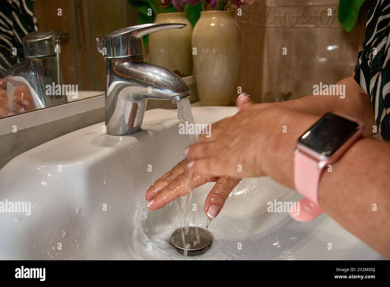 A woman washing her hands under running water in a modern bathroom sink ...