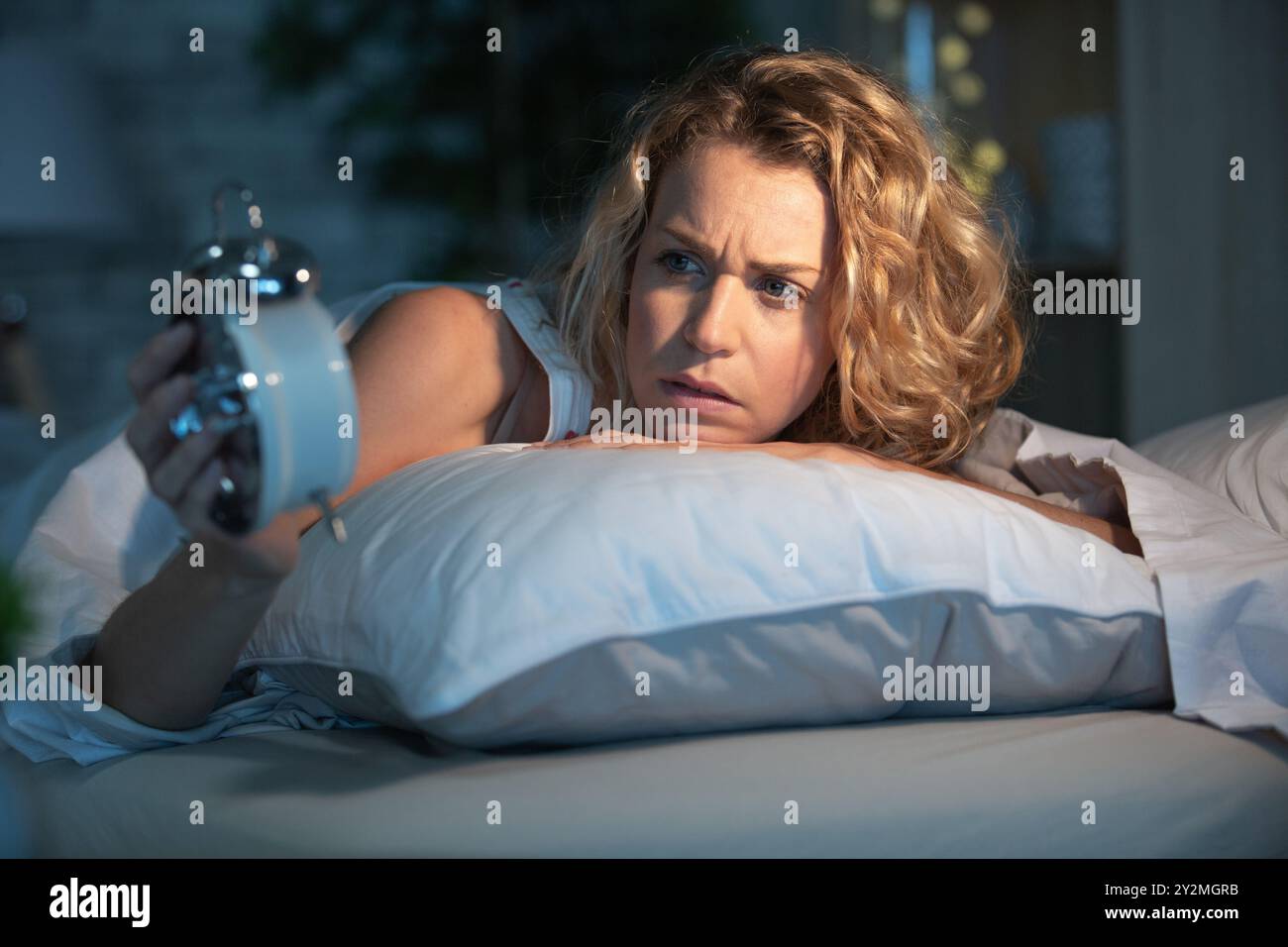 sleepless woman lying in bed looking at her clock Stock Photo - Alamy