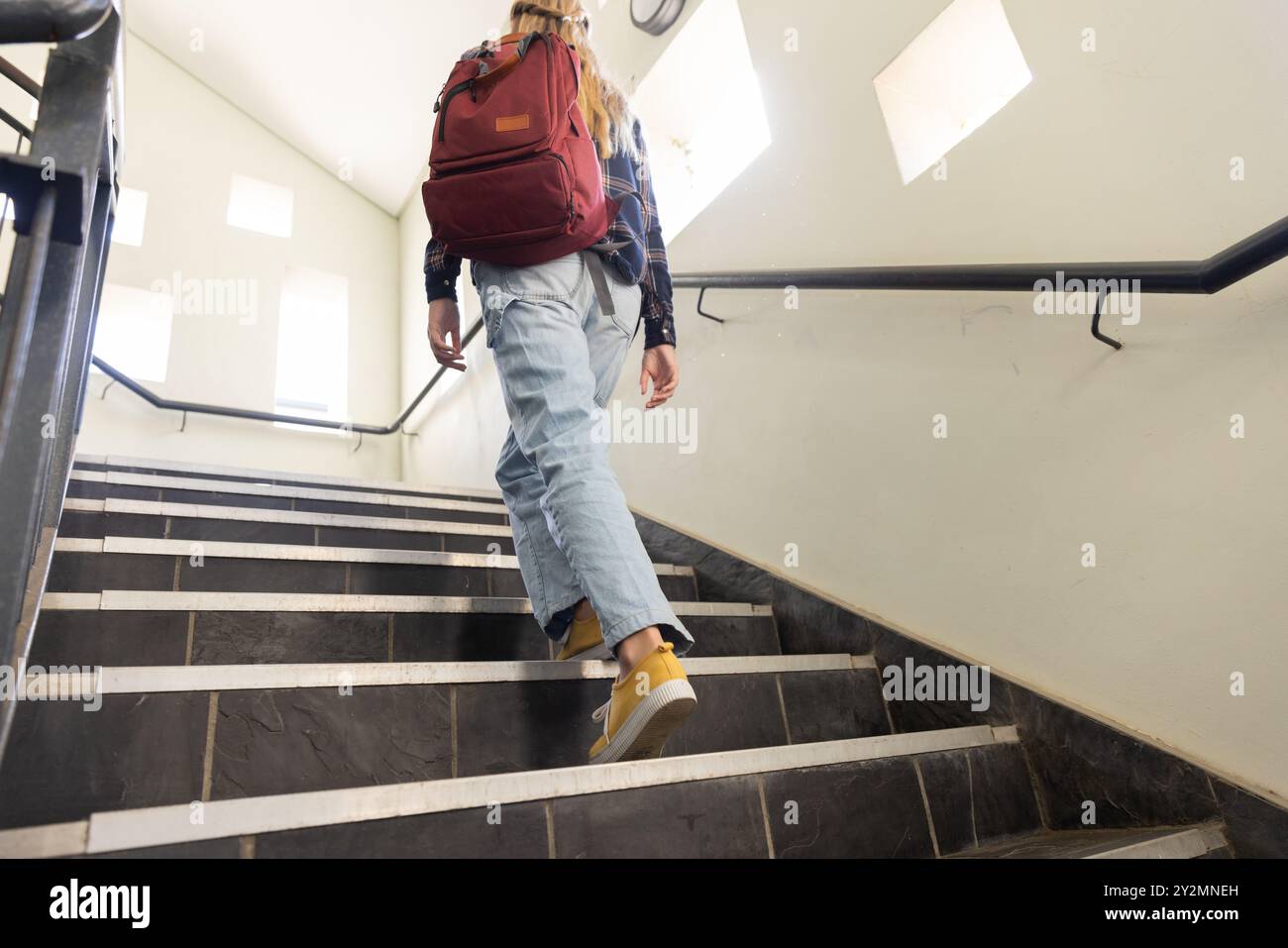 Teenage girl with backpack walking up stairs in school building ...
