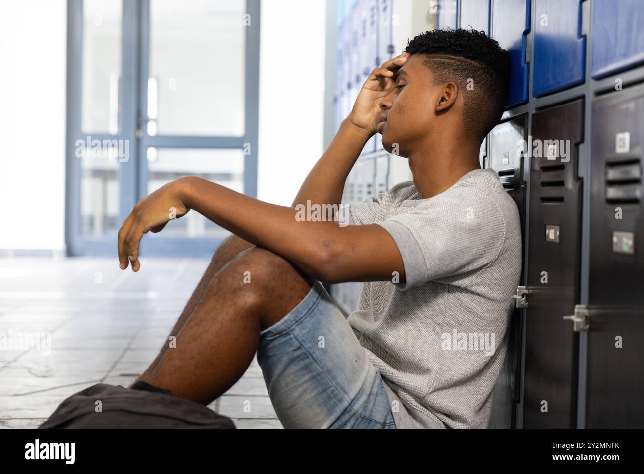 Sitting in school hallway, teenage boy leaning against lockers, looking ...