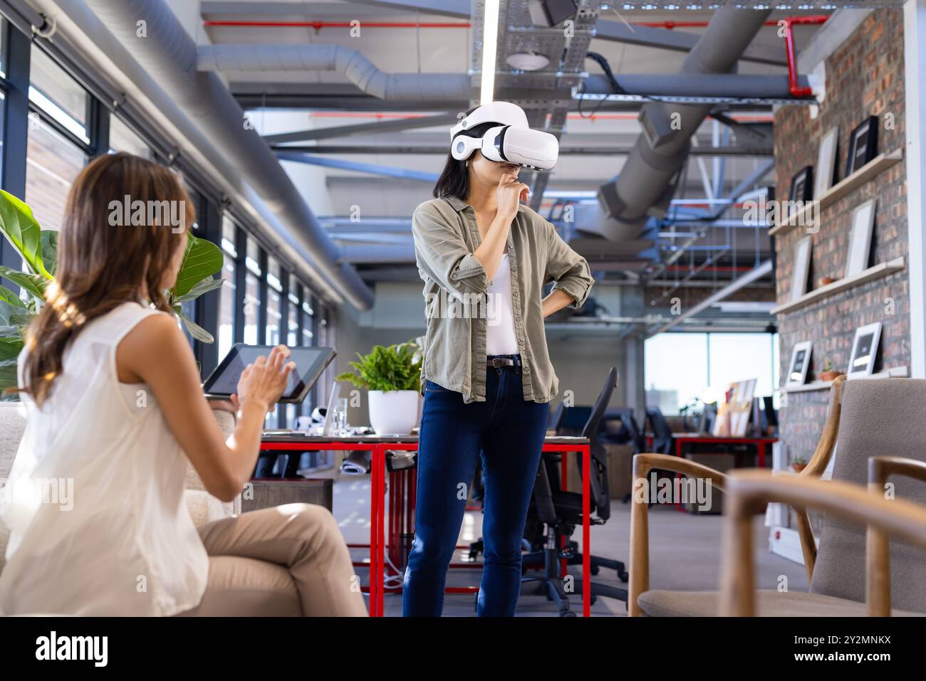 In office, Using VR headset, asian woman exploring virtual interior design while colleague ...