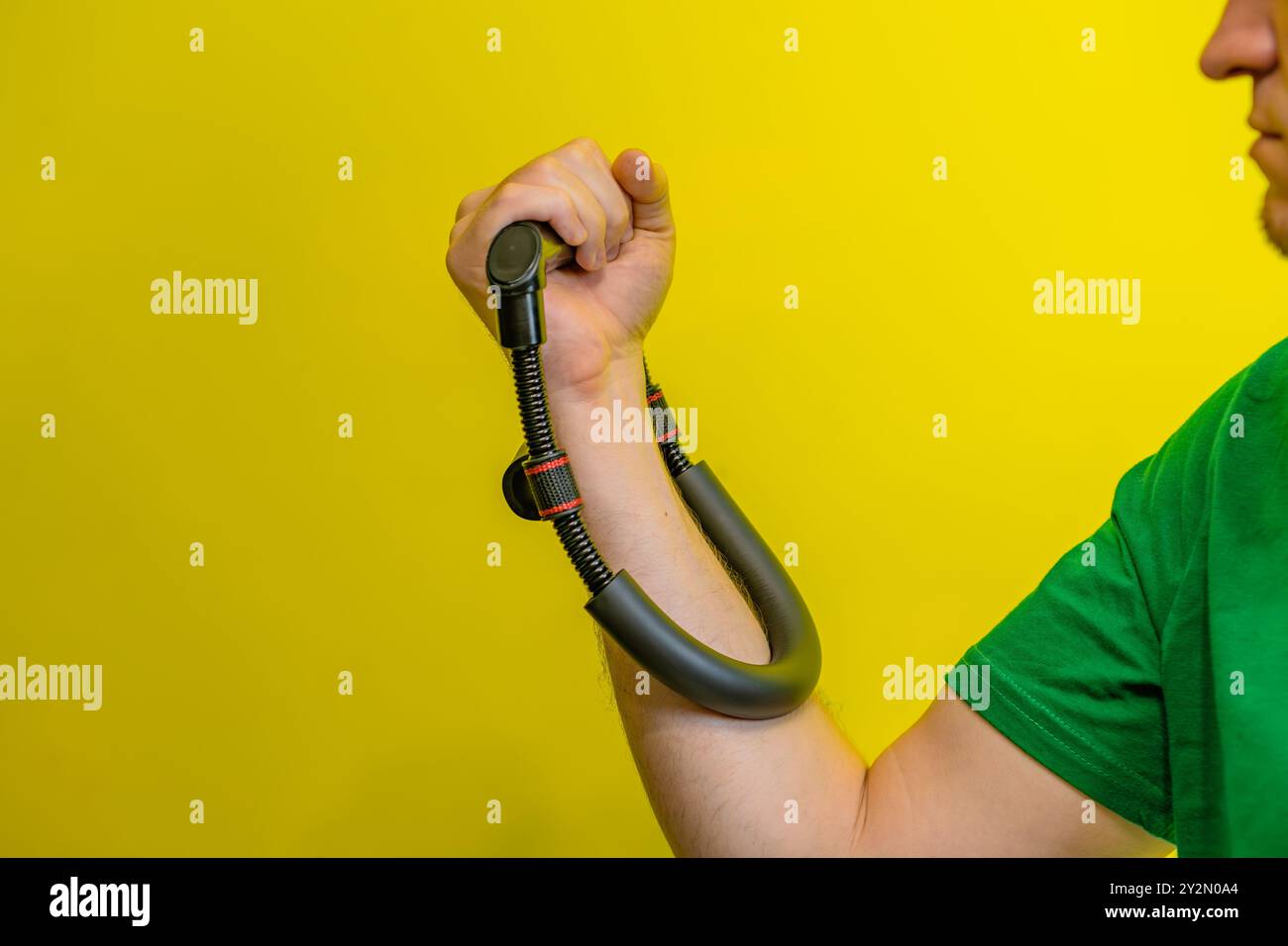A man trains his forearm muscles with a hand grip in front of a yellow ...