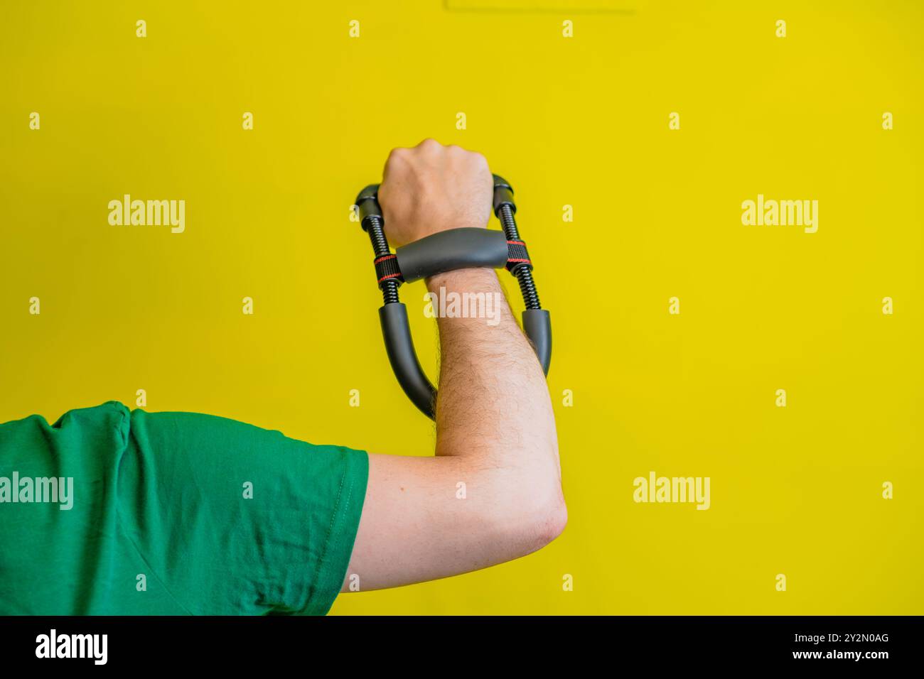 A man trains his forearm muscles with a hand grip in front of a yellow ...