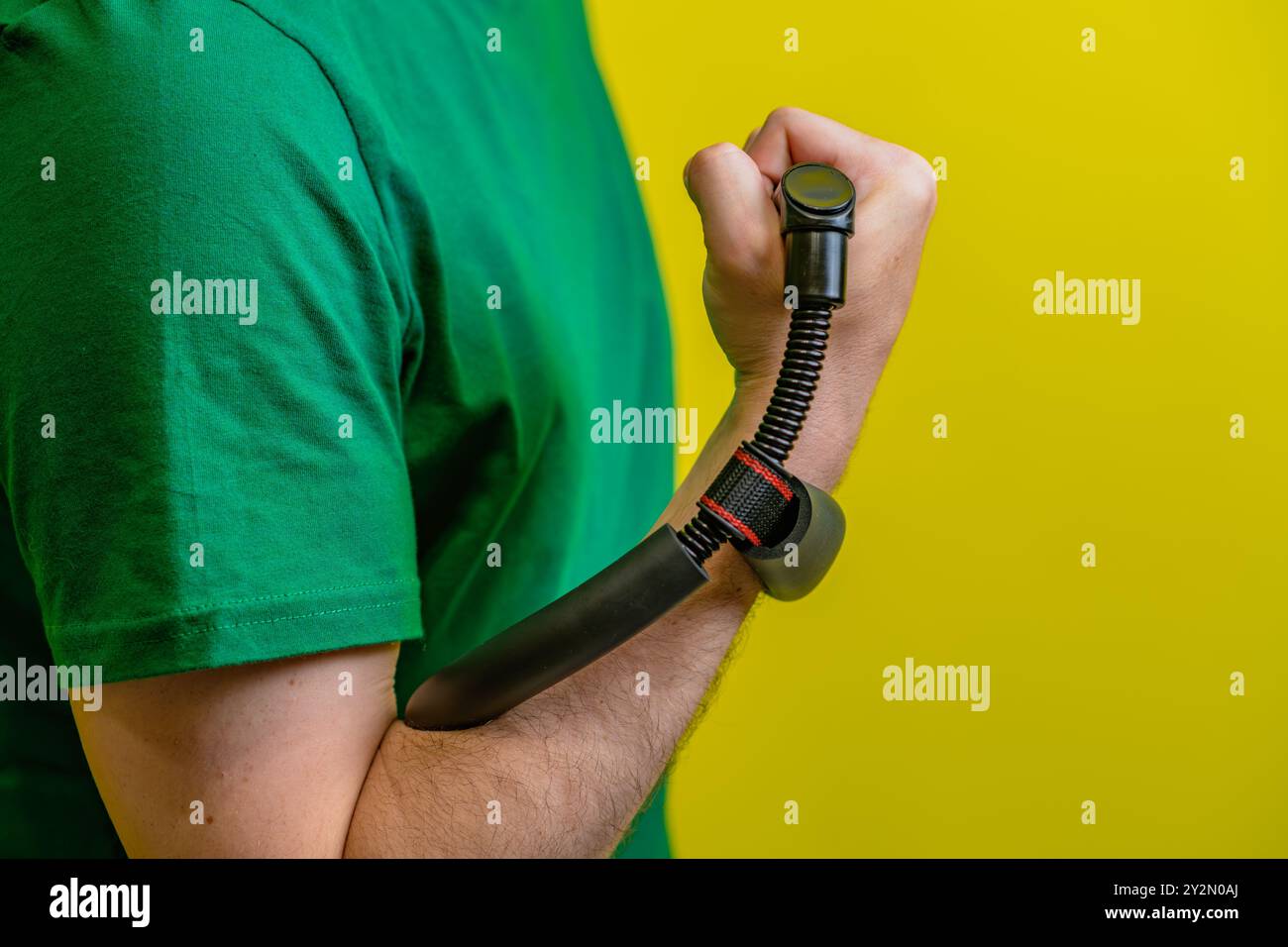 A man trains his forearm muscles with a hand grip in front of a yellow ...