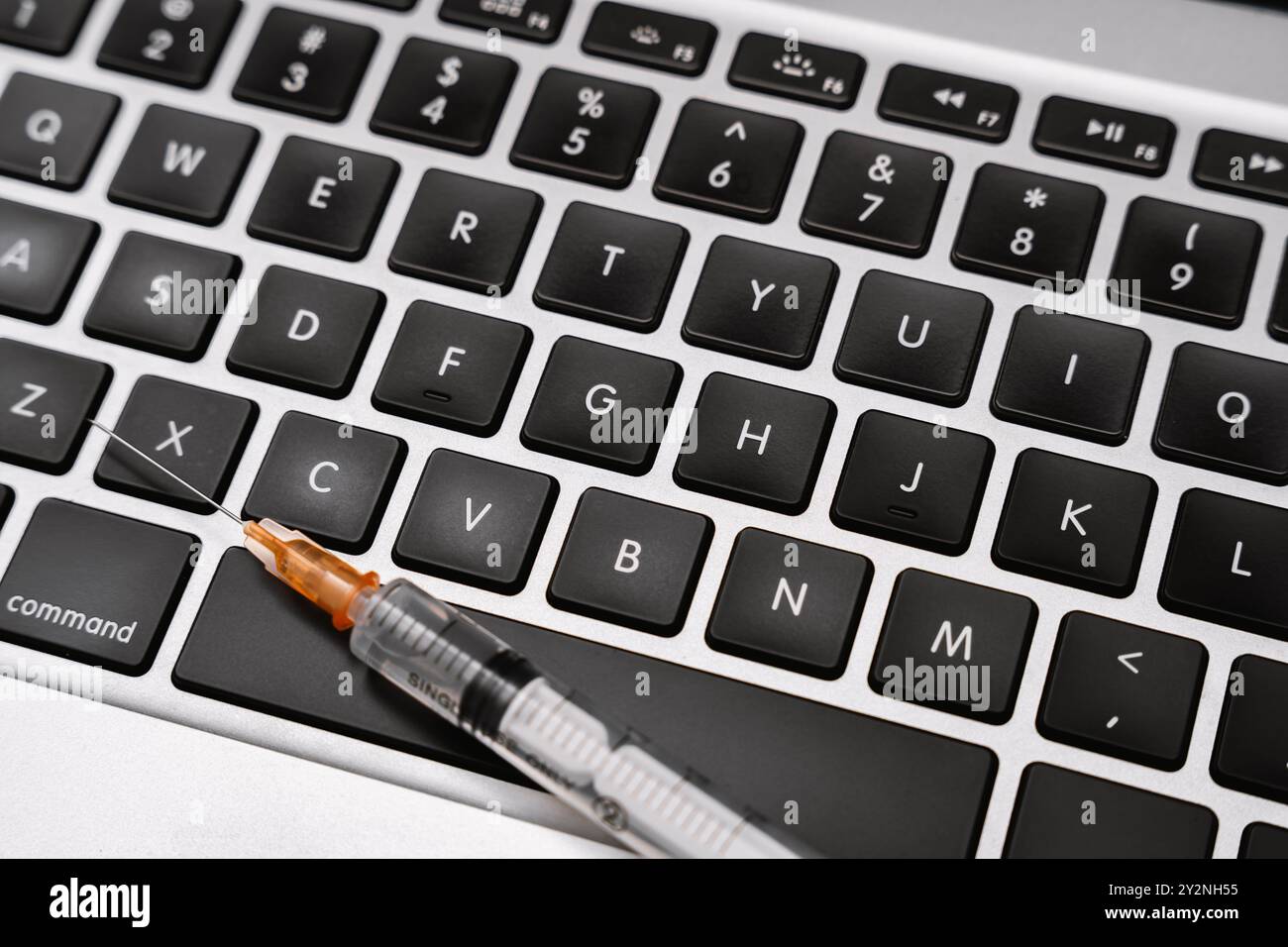 Syringe on Keyboard: A medical syringe rests on a computer keyboard, symbolizing the ...