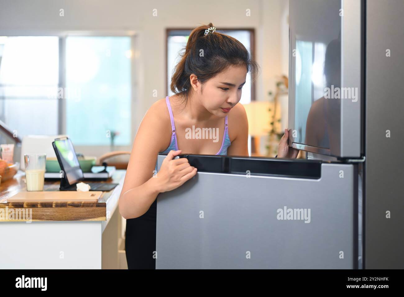 Smiling young woman looking inside the fridge, searching for ...