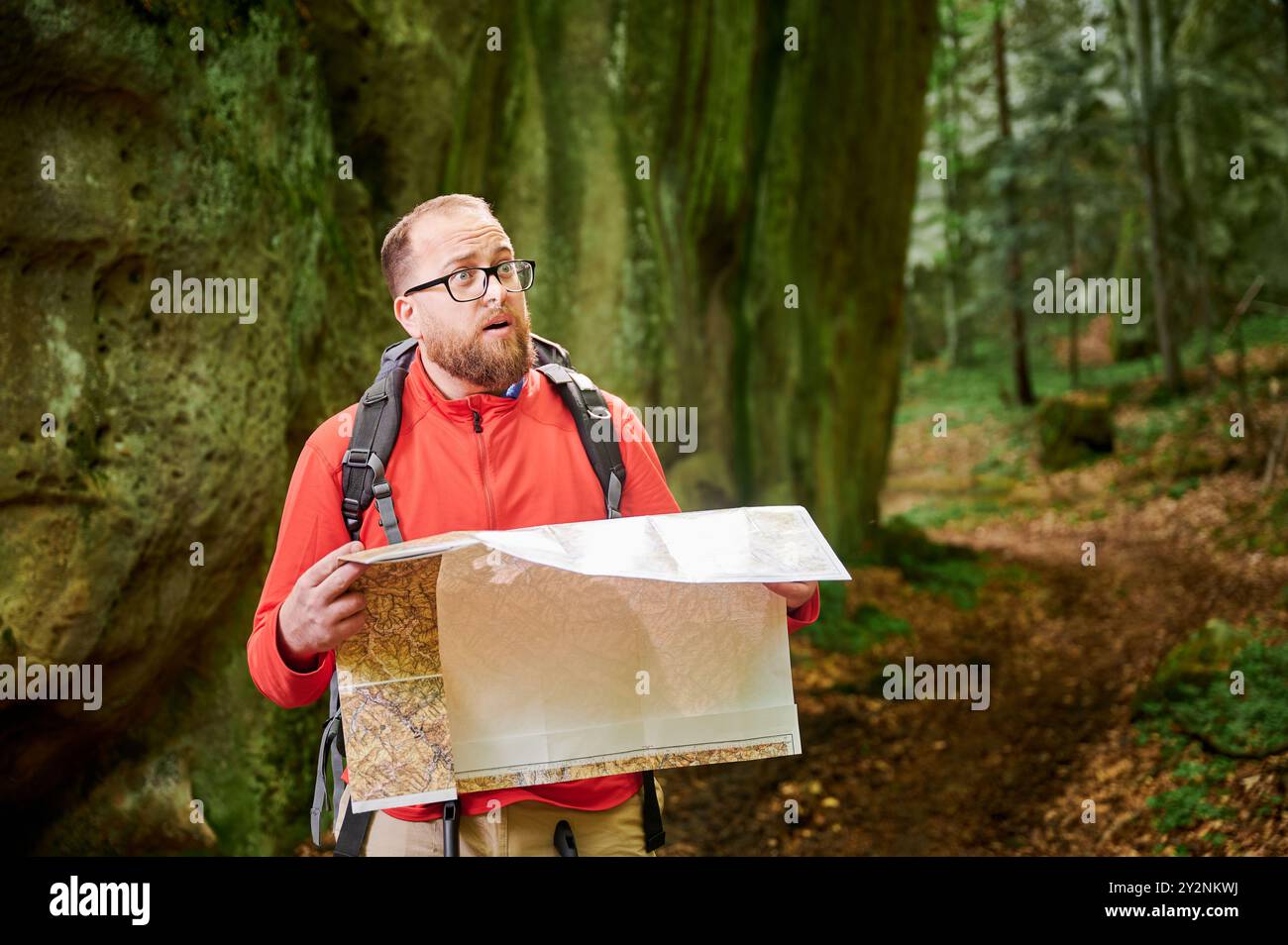 Bearded tourist man with surprised expression studies map while stands ...