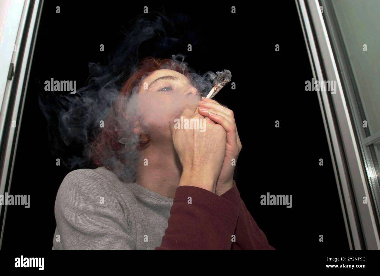 a person smoking a joint, blurred green meadow and blue sky in the back ...