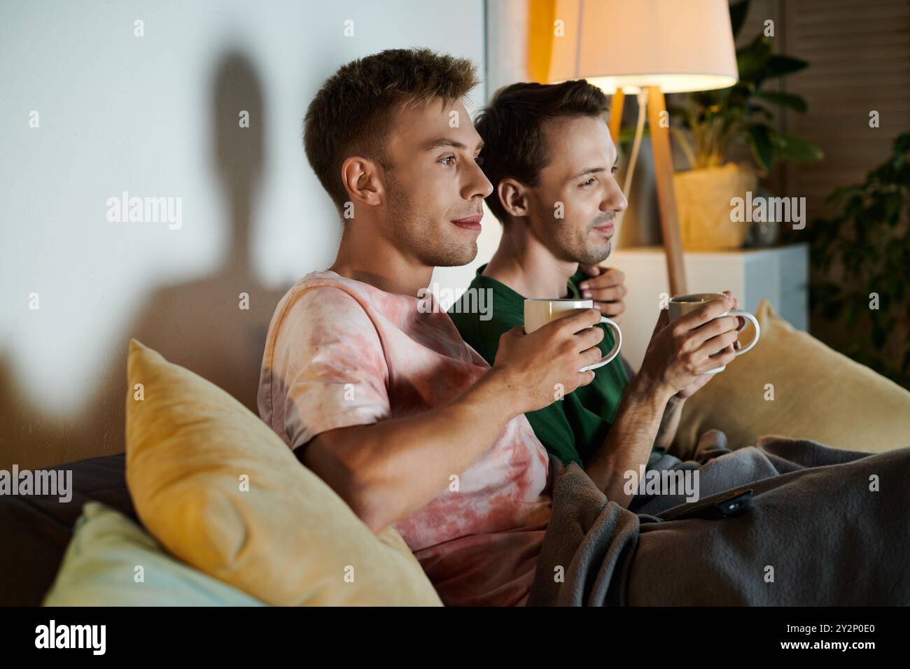 Two men share a joyful moment while sipping drinks on their cozy couch ...