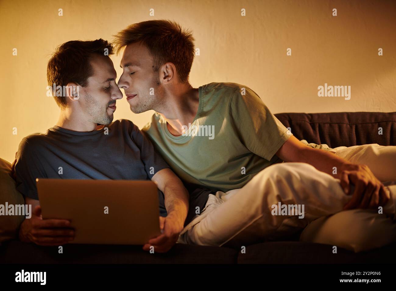 Two men connect intimately on a couch, basking in warm light and ...